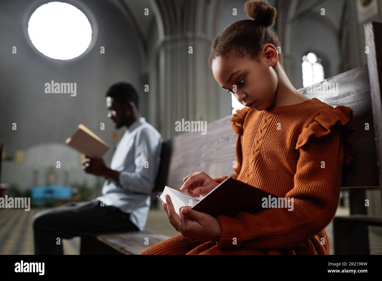 African American little girl reading Bible while sitting on bench in ...