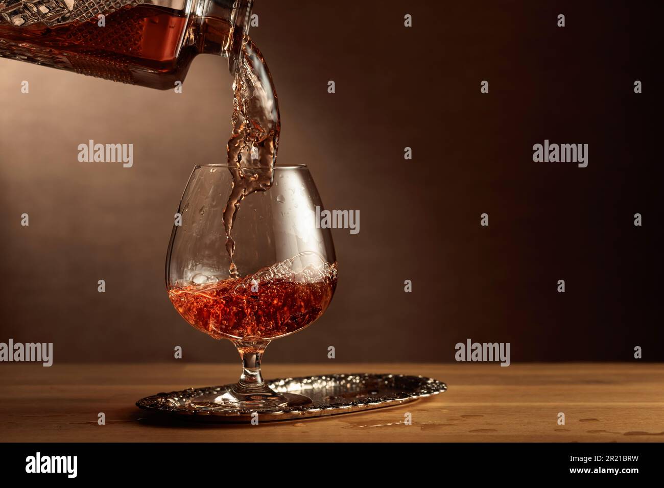 Brandy is poured from a decanter into a snifter glass. Cognac on an oak table. Copy space Stock ...