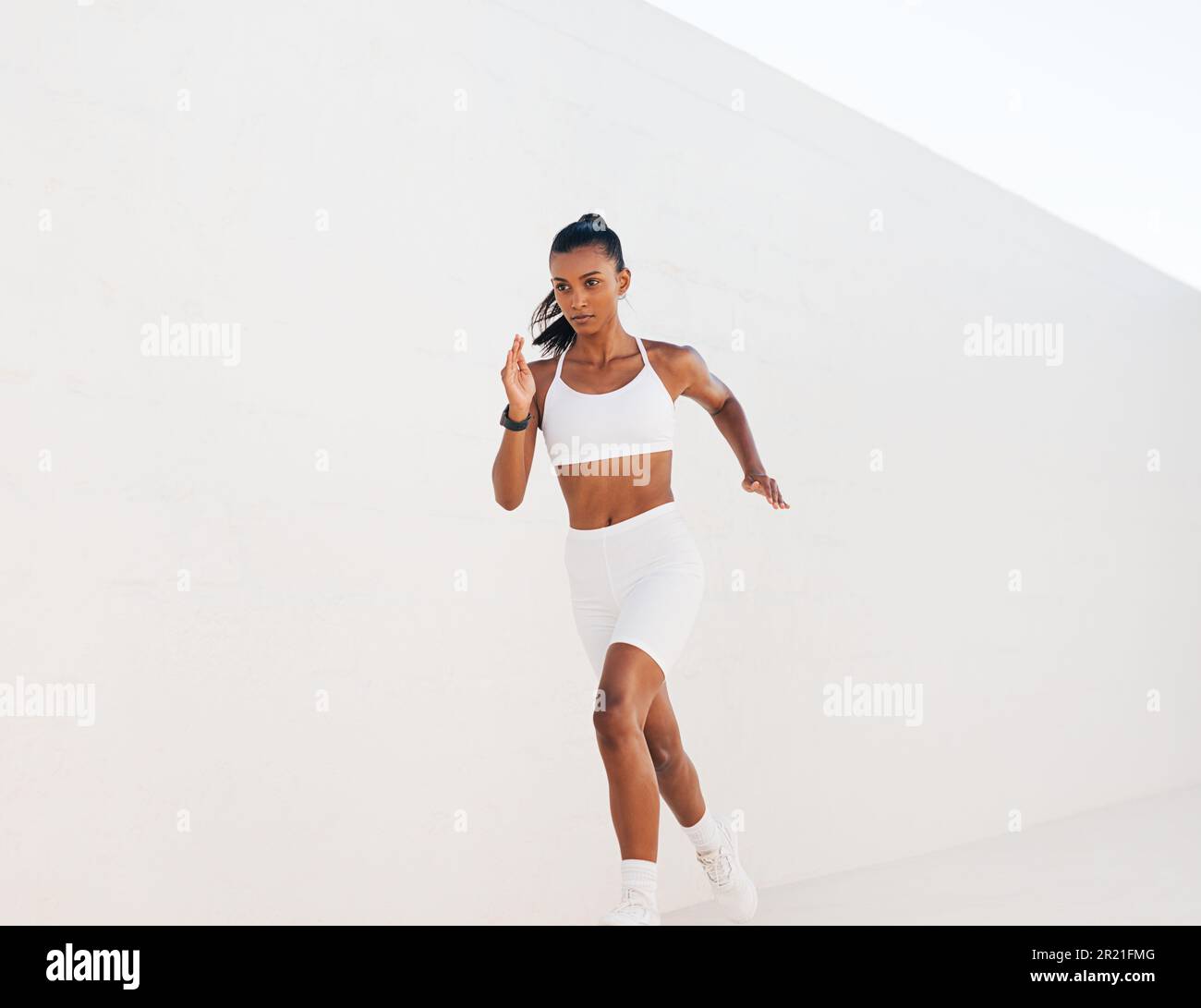 Young jogger running against a white wall outdoors. Muscular woman ...