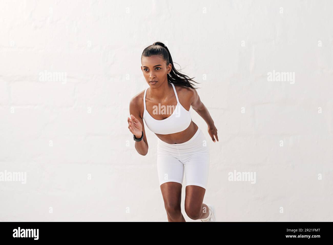 Young slim female athlete running outdoors against a white wall ...
