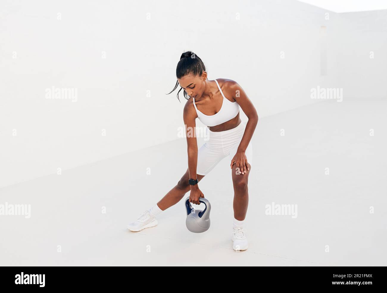 Slim female in a white sports bra doing intense training with a ...