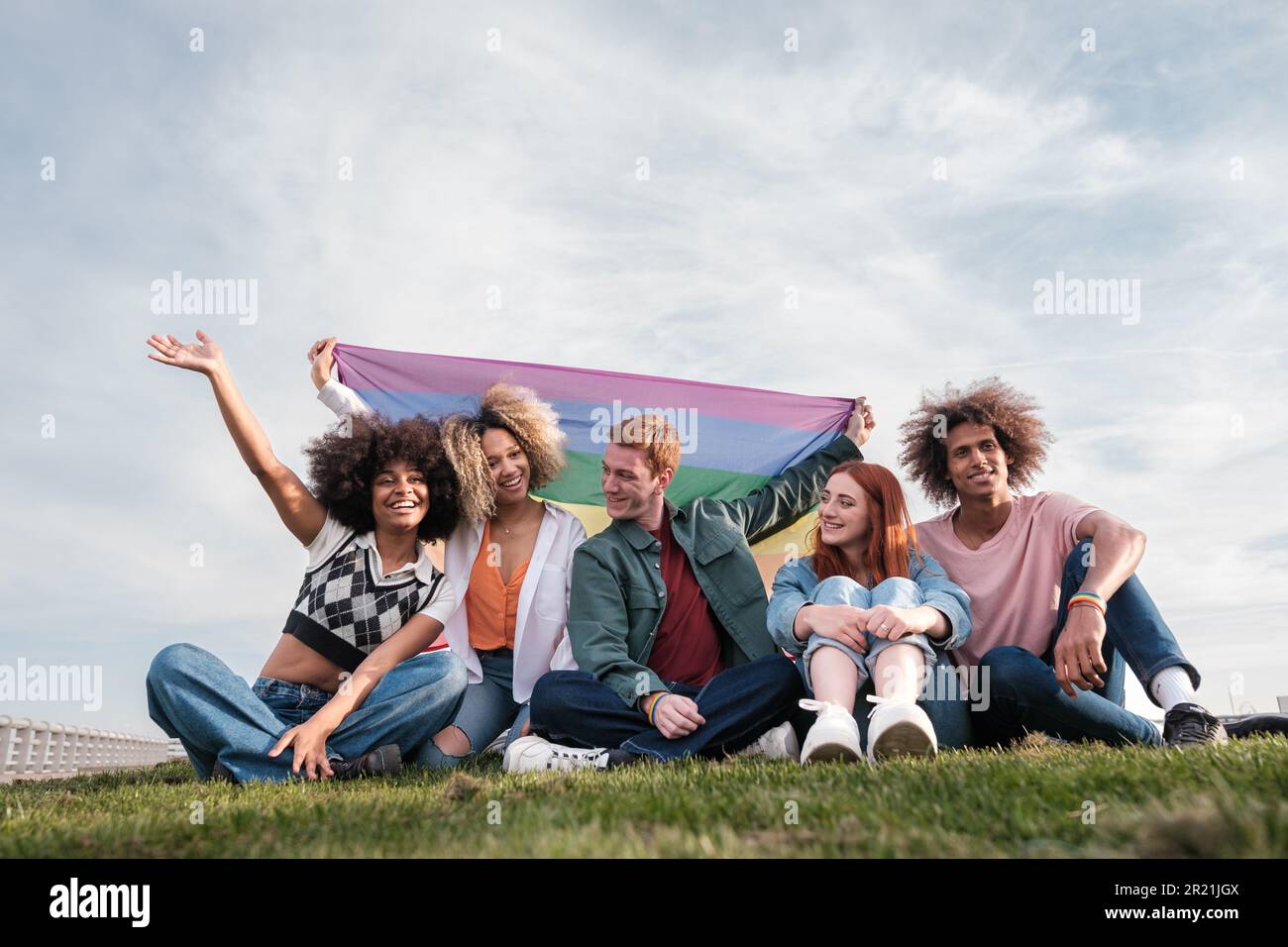 Young people at sunset sitting on the grass and raising the lgtbi flag ...
