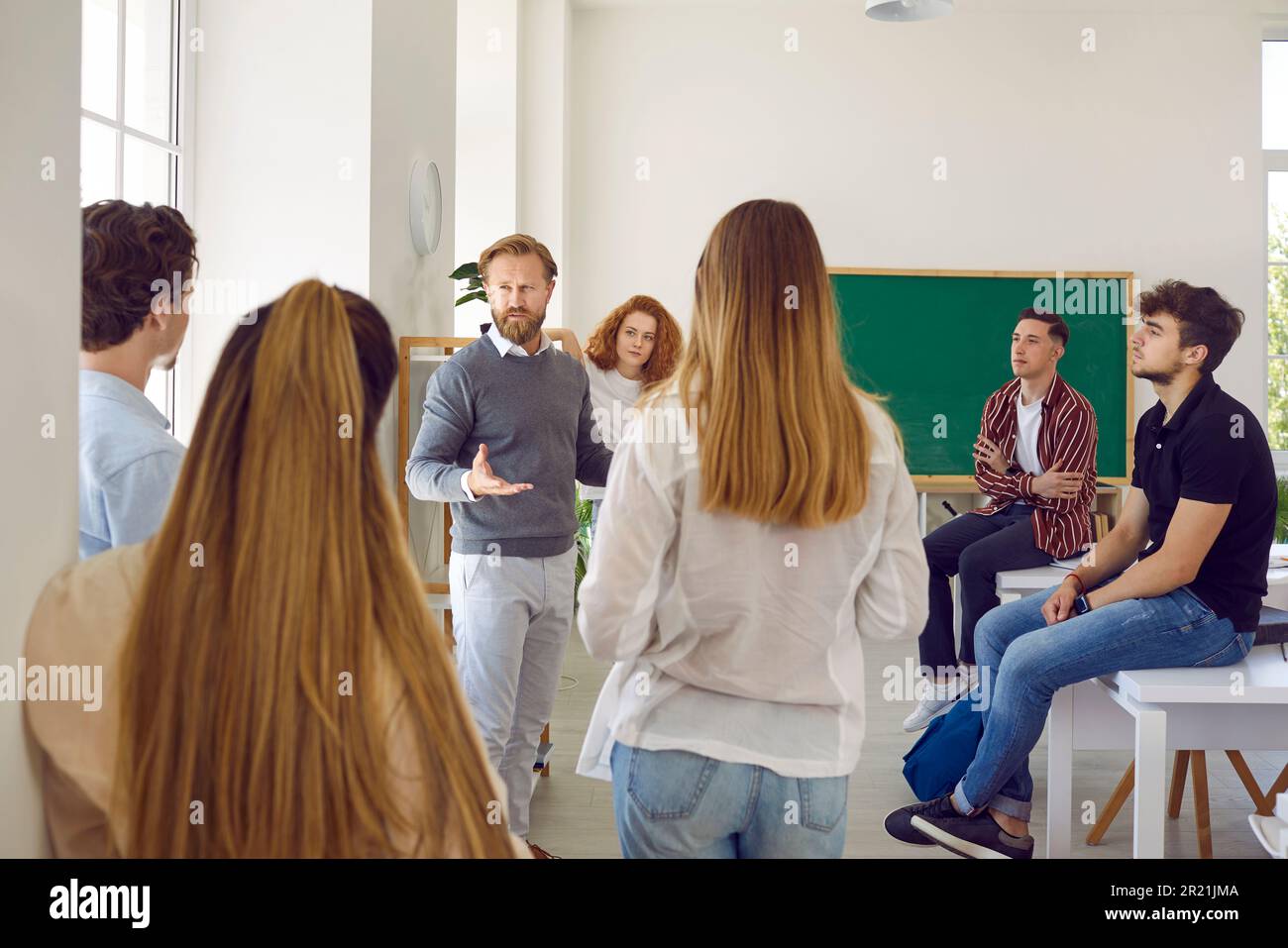 Smart and intelligent male teacher speaks in classroom surrounded by his high school students ...