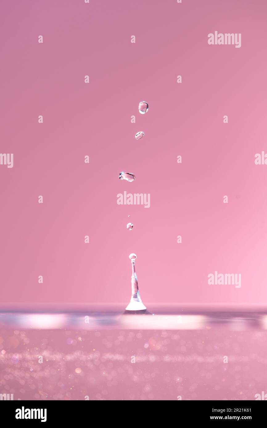Water droplets fall down closely into the pink water, making it the ...