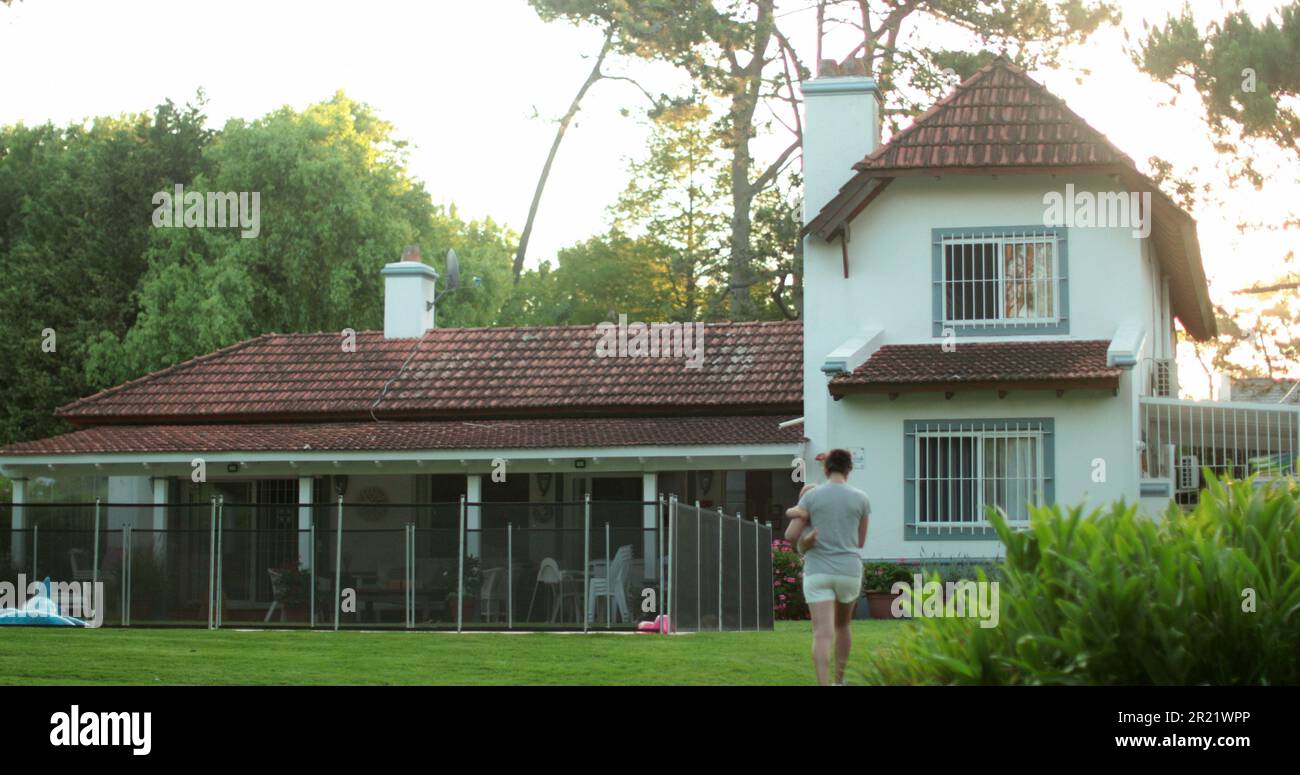 Exterior of residential home and mother carrying baby walking towards ...