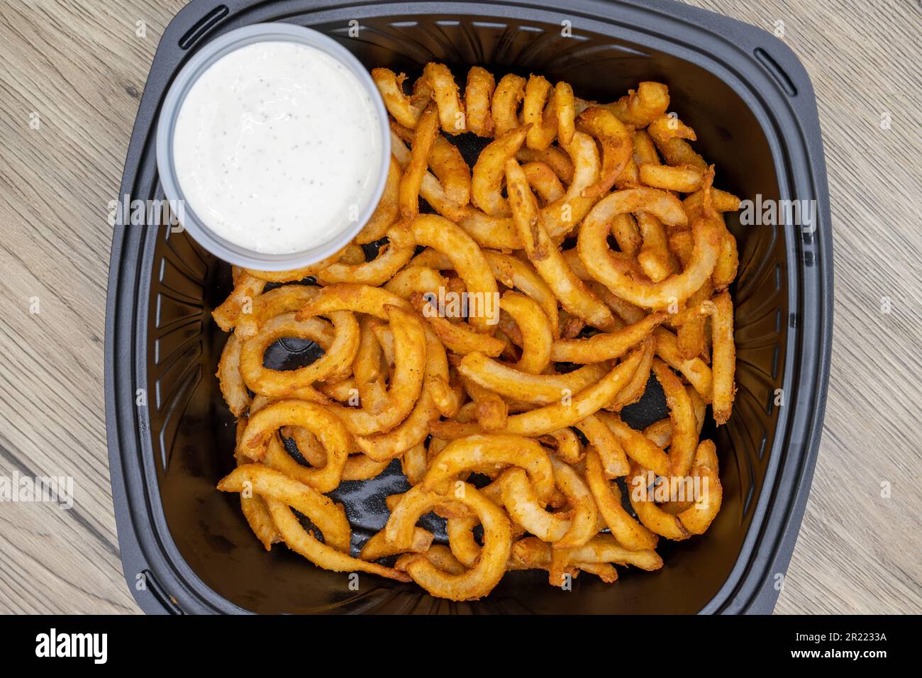 Overhead view of to go order of crispy curly fries packed in plastic ...