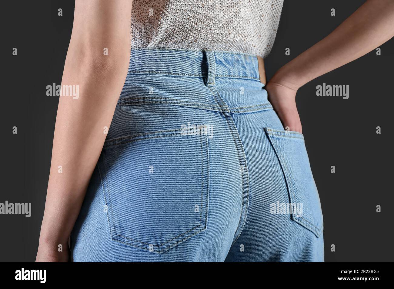 Young woman in stylish jeans on dark background, back view Stock Photo ...