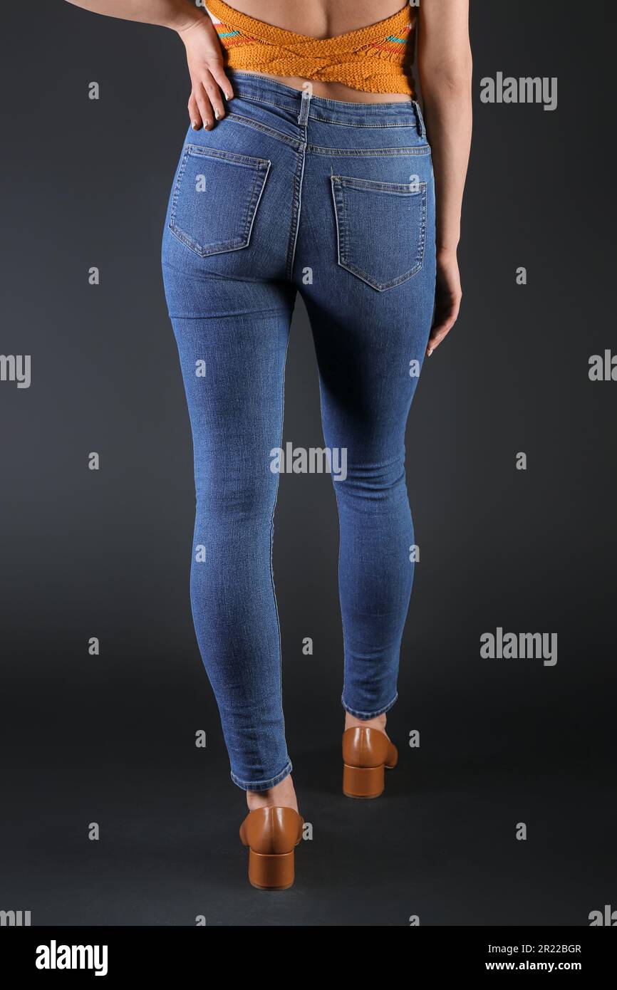 Young woman in skinny jeans on dark background, back view Stock Photo ...