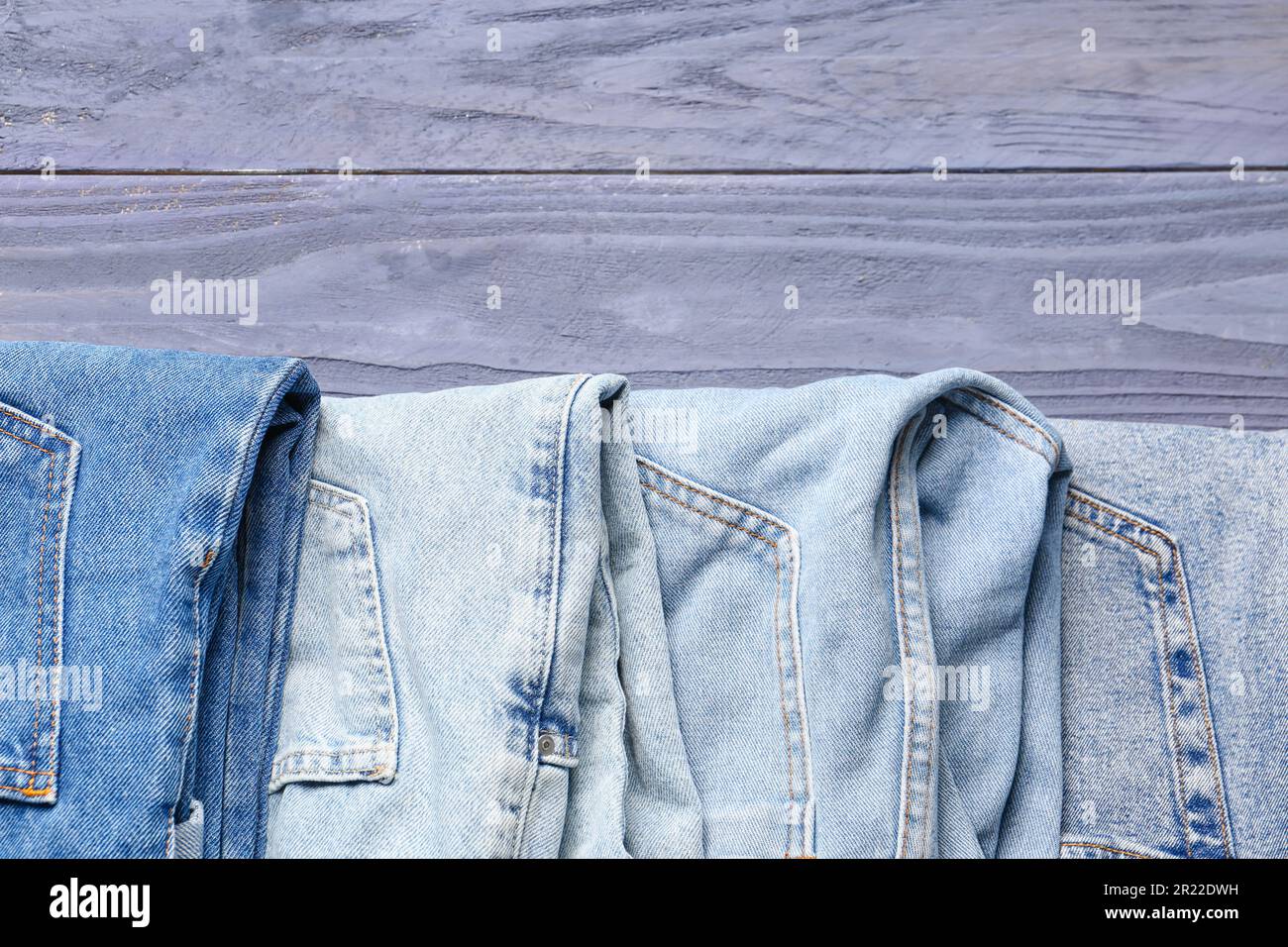 Different folded denim jeans on blue wooden background Stock Photo - Alamy