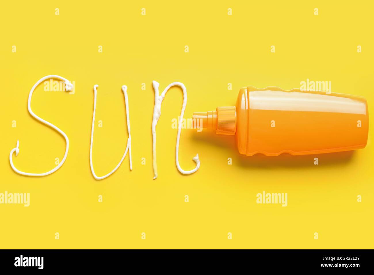 Bottle with sunscreen and word SUN made of cream on yellow background ...