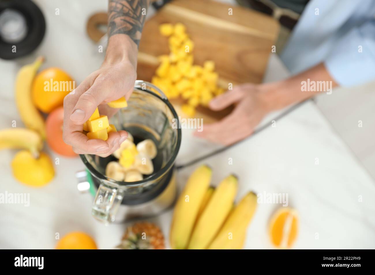 Man adding mango into blender with ingredients for smoothie, top view ...
