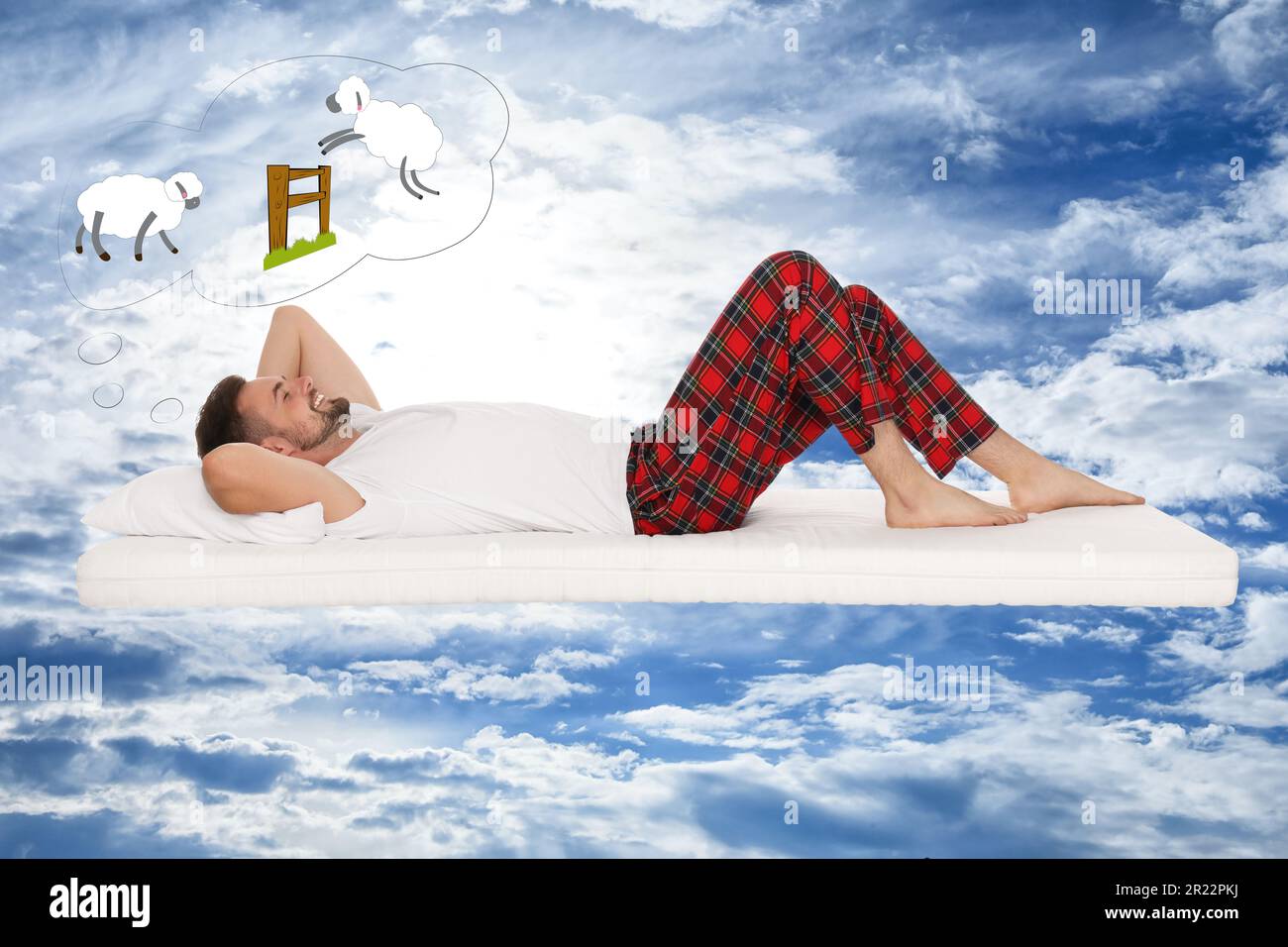 Sweet dreams. Young man lying on matress and counting sheep jumping over fence in blue sky with ...