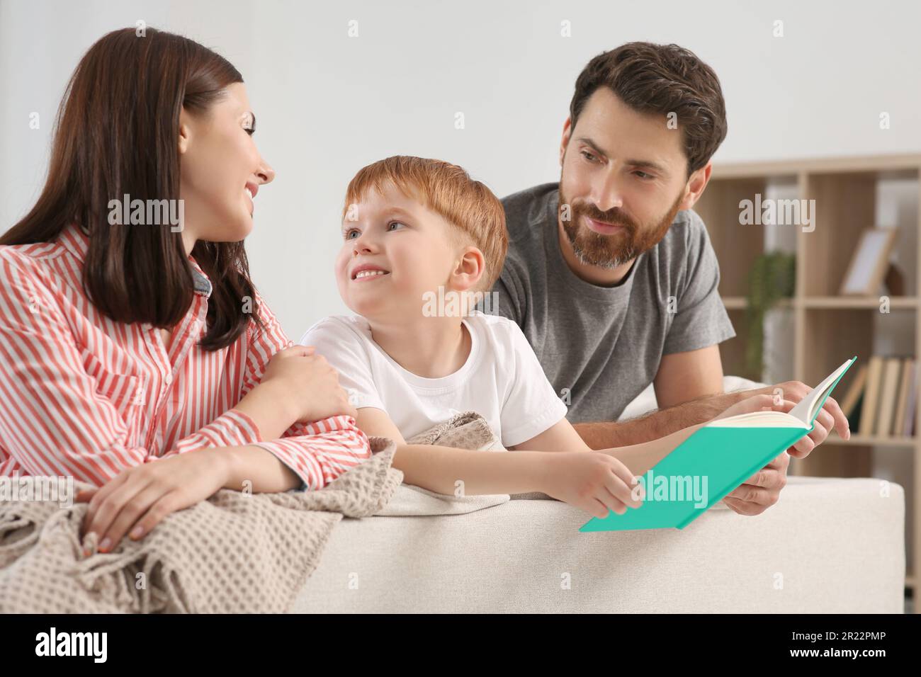Happy parents with their child reading book on couch at home Stock ...
