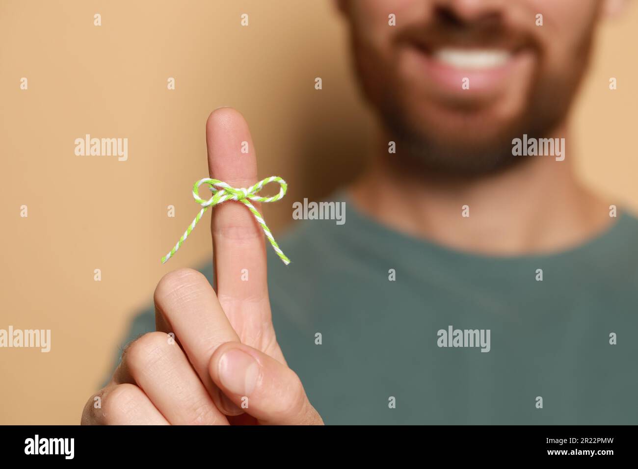 Man showing index finger with tied bow as reminder against beige ...