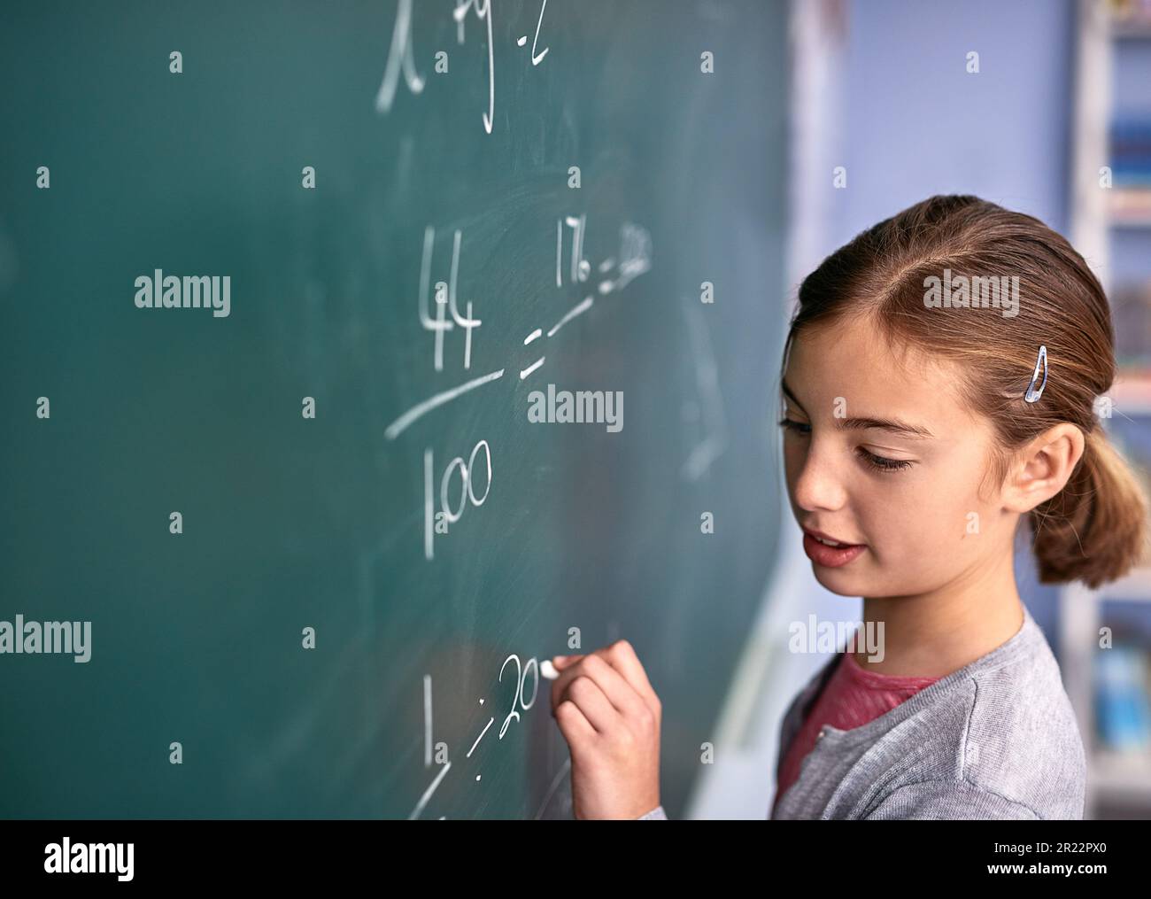 Shes almost got it. an elementary school girl writing on a blackboard ...
