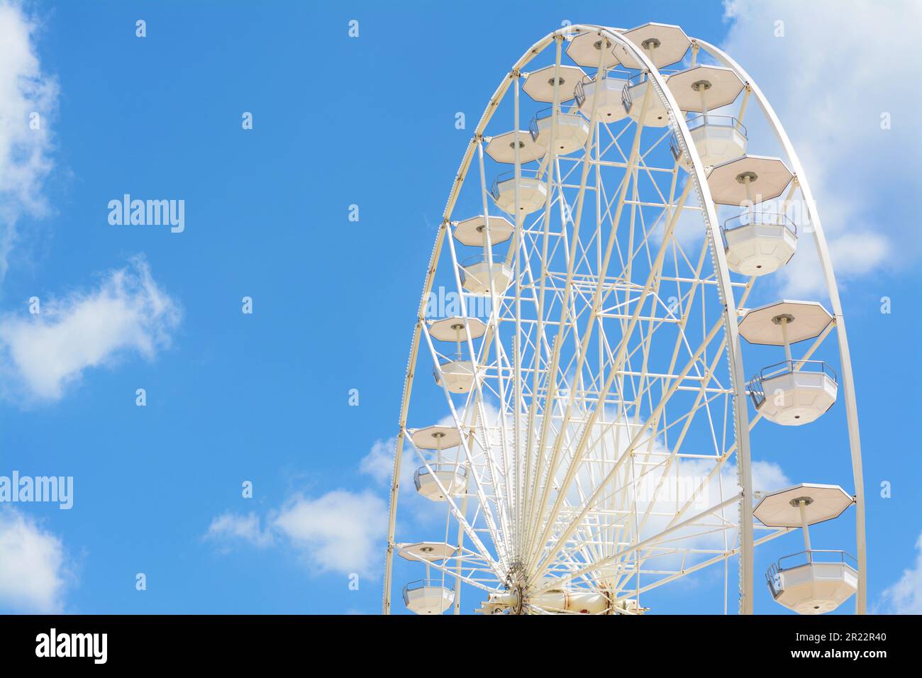 Large white observation wheel against blue cloudy sky, space for text ...