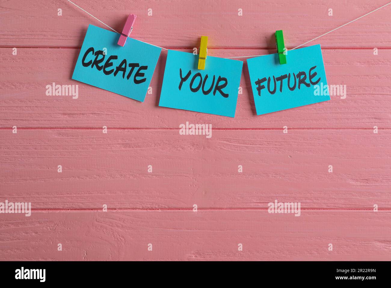 Paper notes with motivational phrase Create Your Future hanging on pink ...