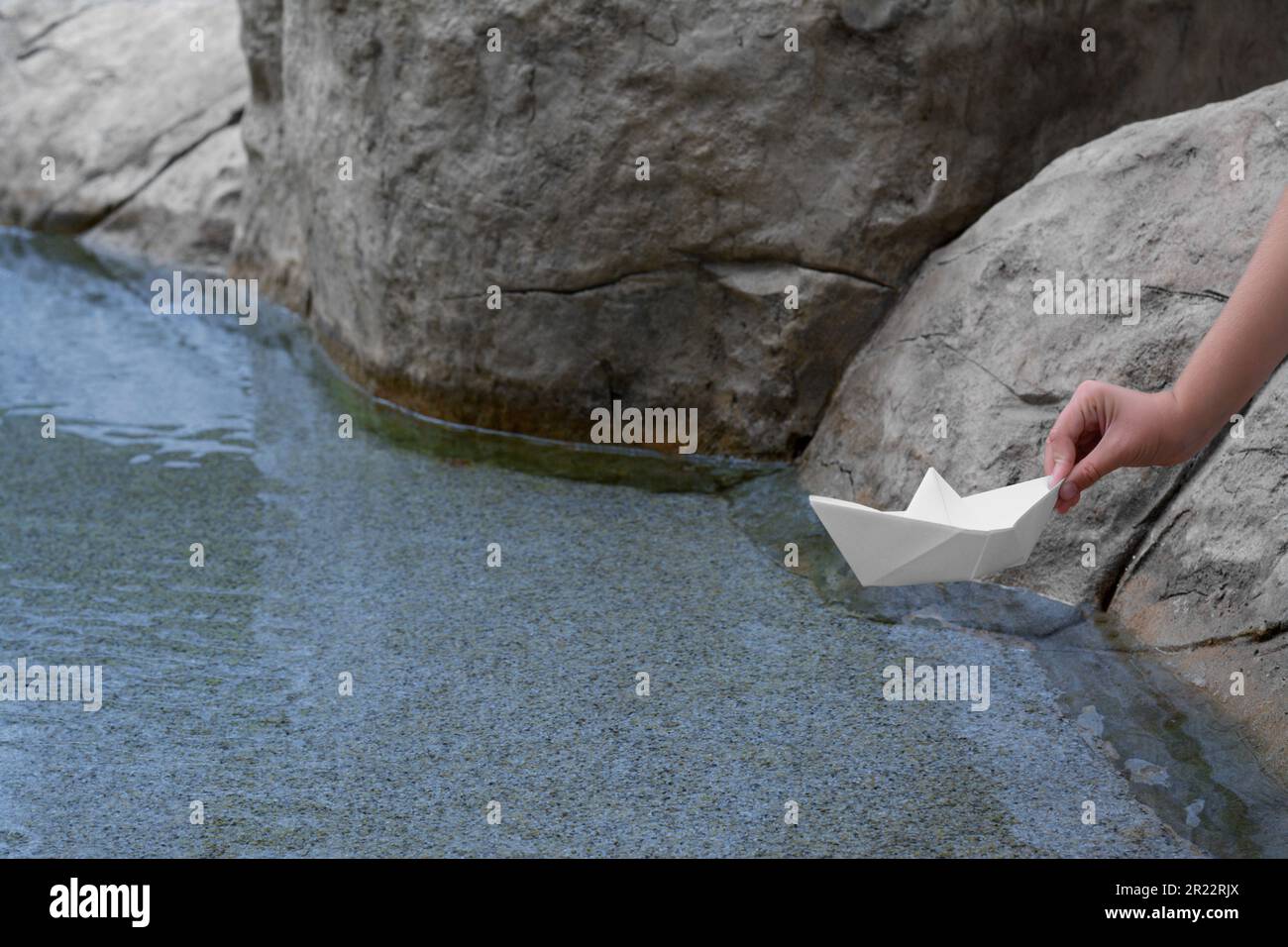 Kid launching small white paper boat on water outdoors, closeup. Space ...