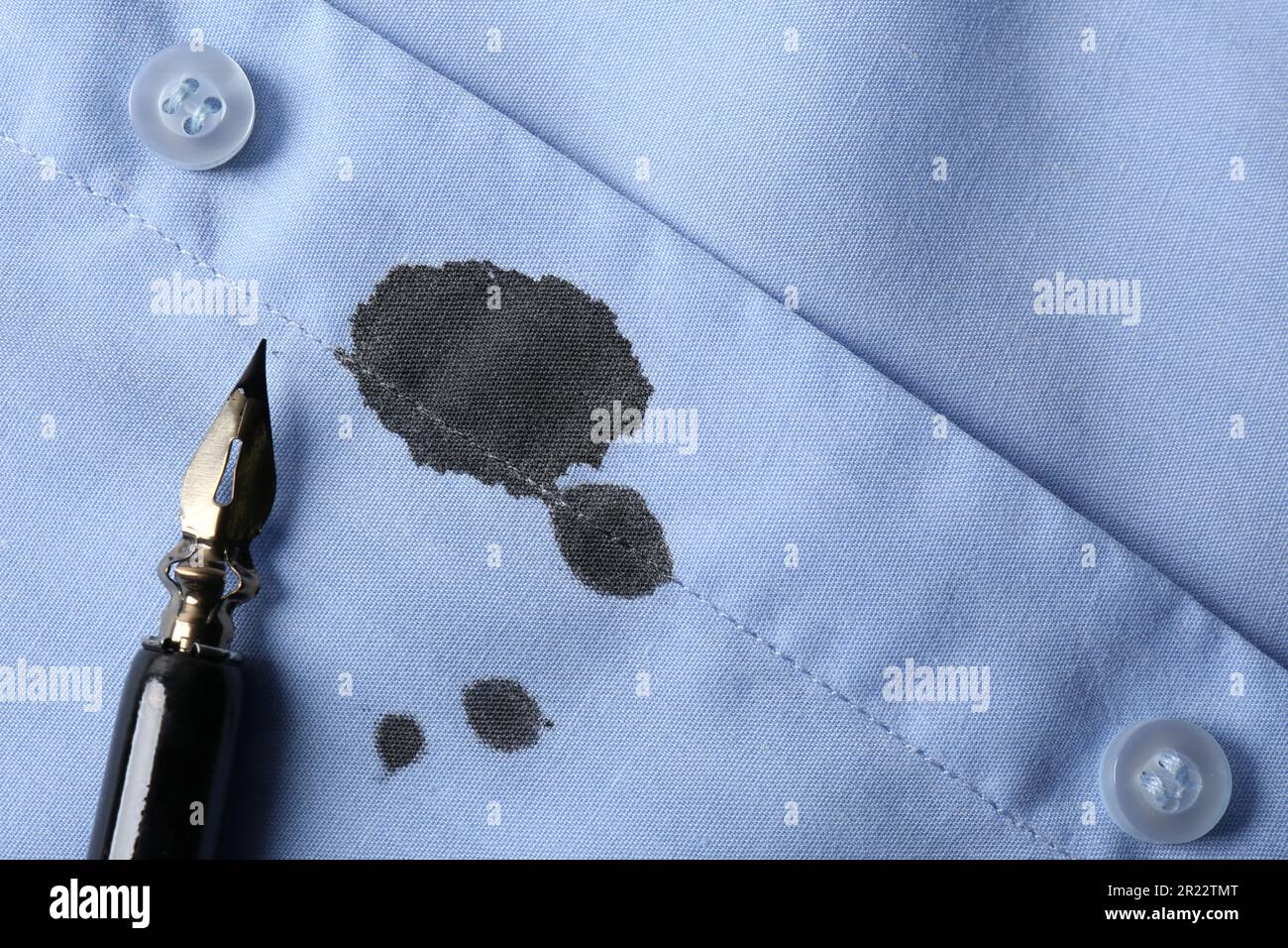 Black ink stain on light blue shirt and pen, top view. Space for text ...