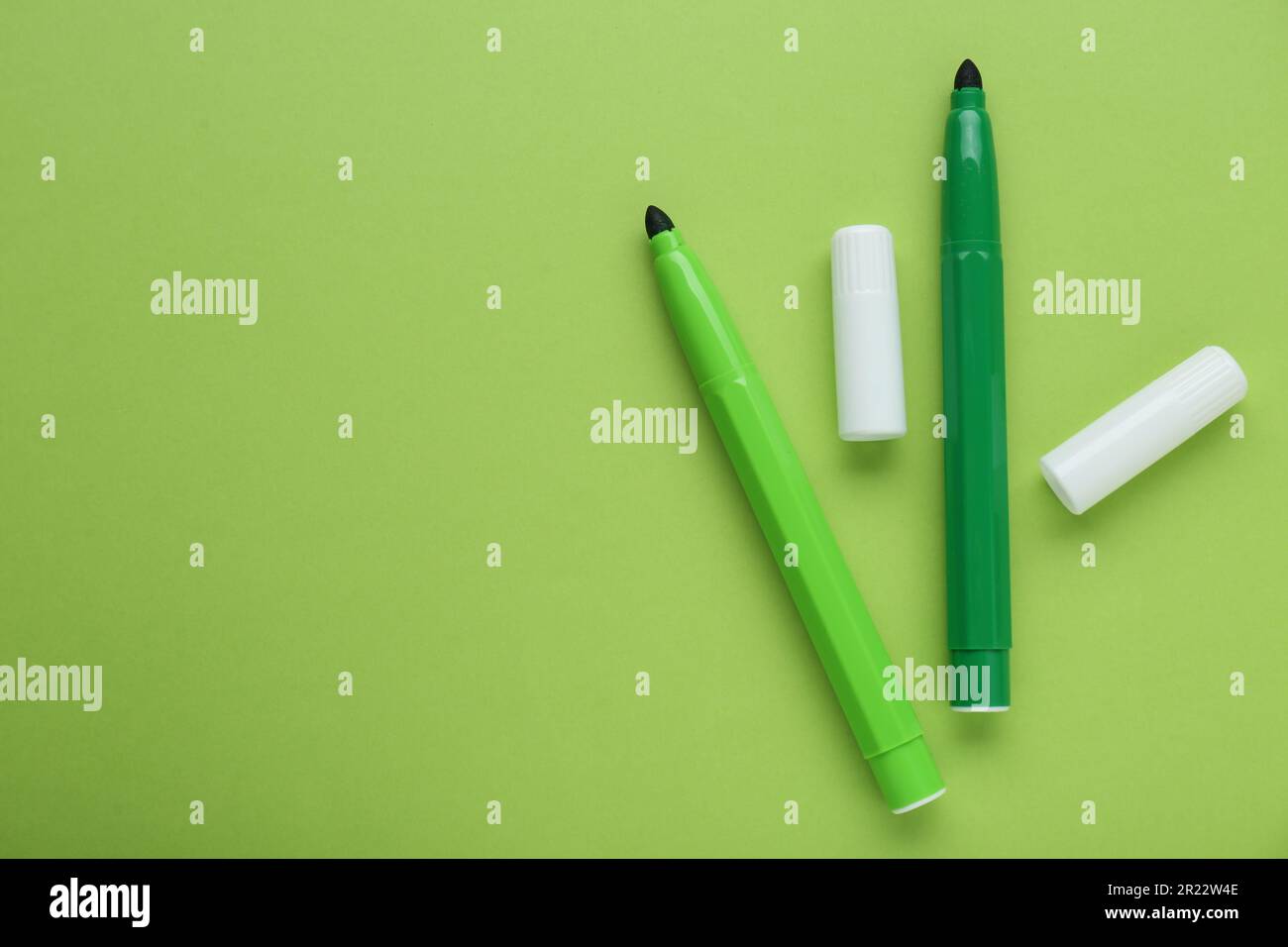 Bright markers and caps on light green background, flat lay. Space for ...