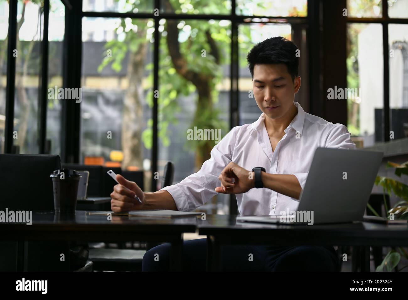 Smart and handsome Asian businessman checking time on his wristwatch ...