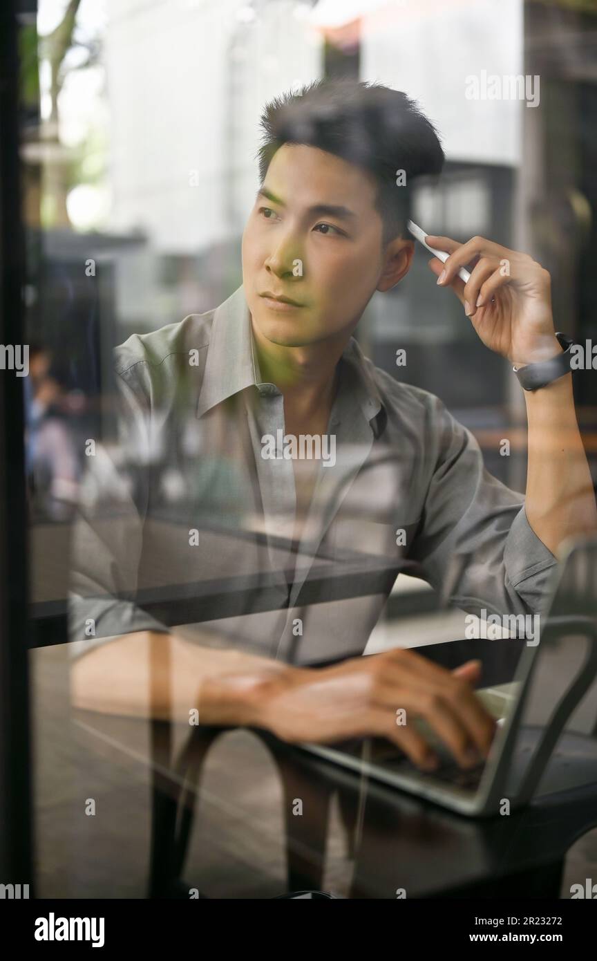 Portrait of a handsome and thoughtful millennial Asian businessman sits ...
