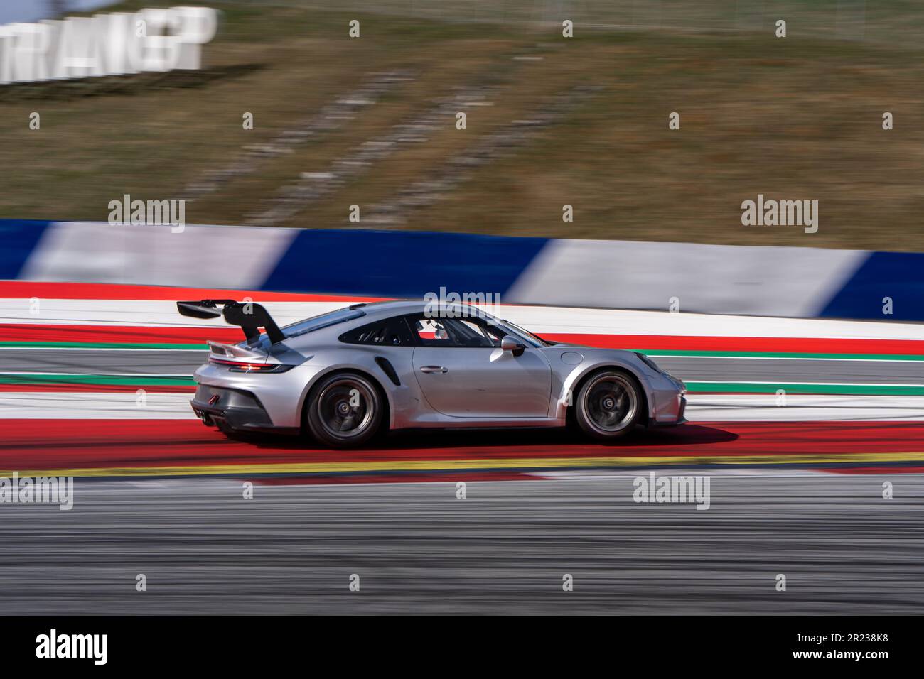 A sleek silver sports car racing along a winding track, with a hill ...