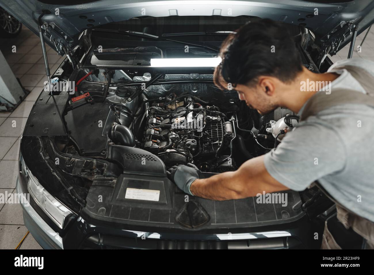 Young male mechanic examining engine under hood of car at the repair ...