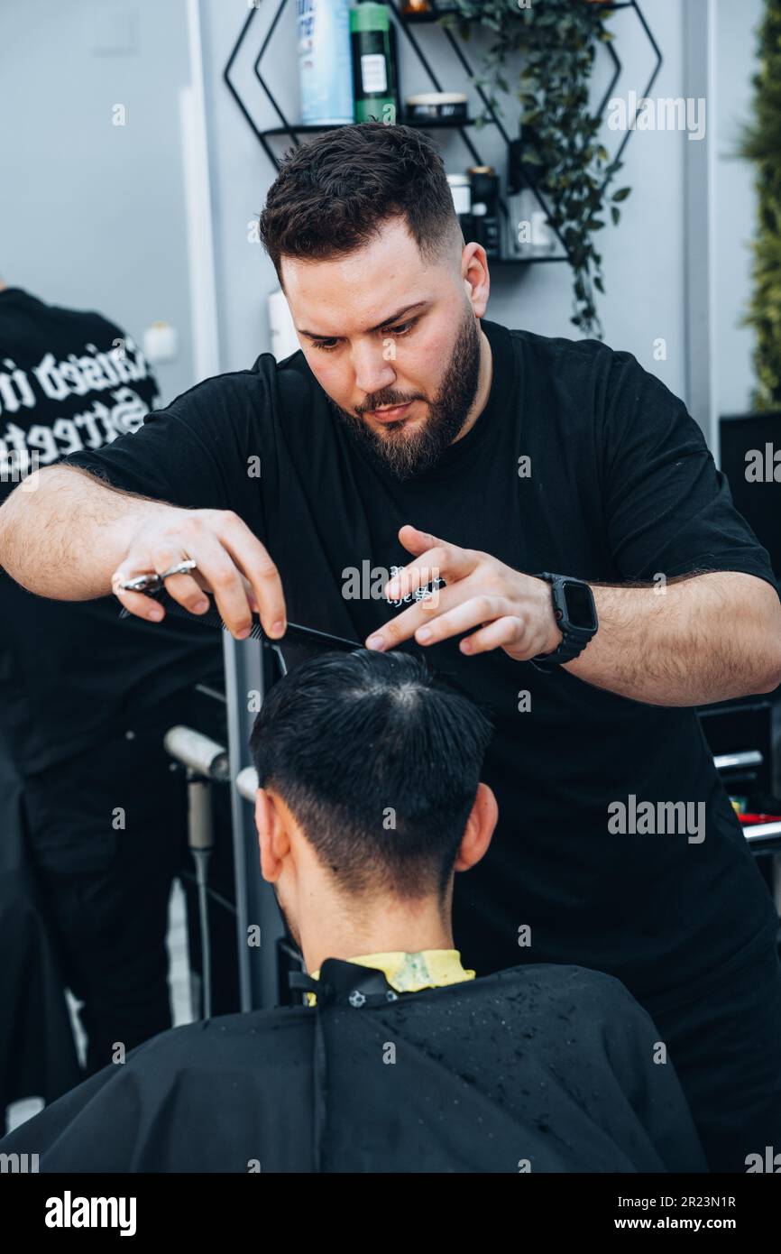 A vertical of a barber trimming a male customer's hair in a salon Stock ...