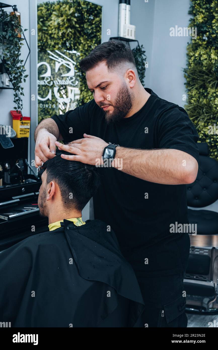 A vertical of a barber trimming a male customer's hair in a salon Stock ...