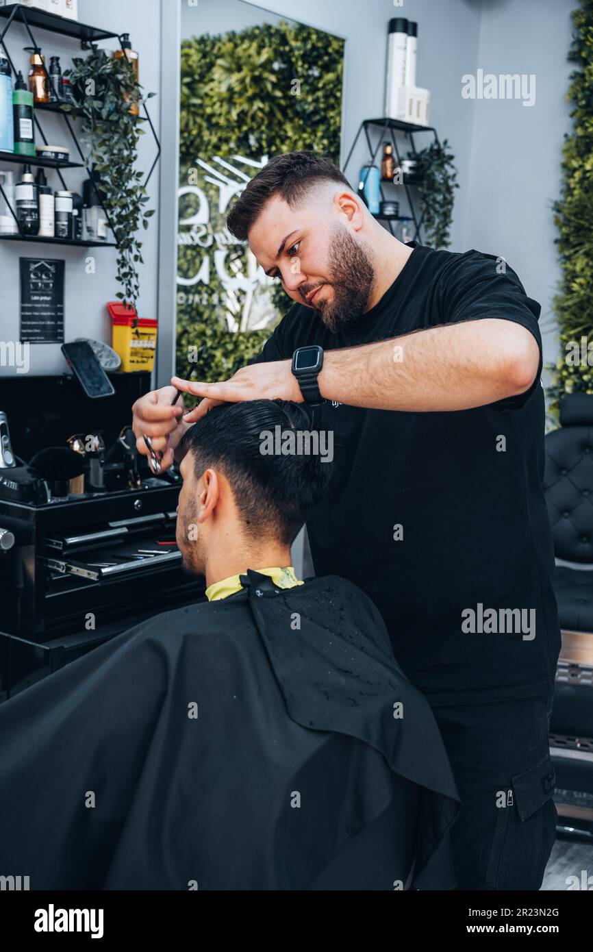 A vertical of a barber trimming a male customer's hair in a salon Stock ...