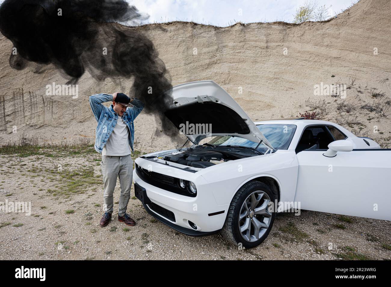 Shocked man is standing near his broken muscle car, open hood, smoke ...