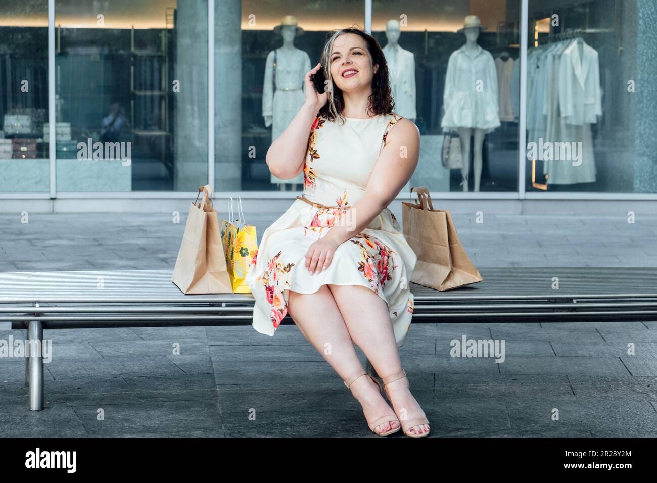 Plus size woman with shopping bags talking by cell phone on shop window ...