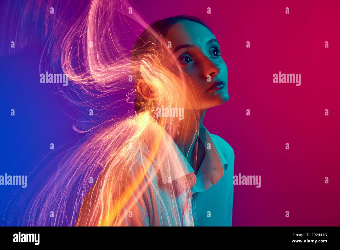 Portrait of young girl posing over gradient blue pink studio background with neon lights effect ...