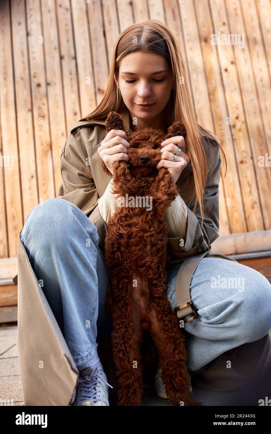A young smiling blonde girl in jeans and a beige raincoat sits and ... A young smiling blonde girl in jeans and a beige raincoat sits and ...