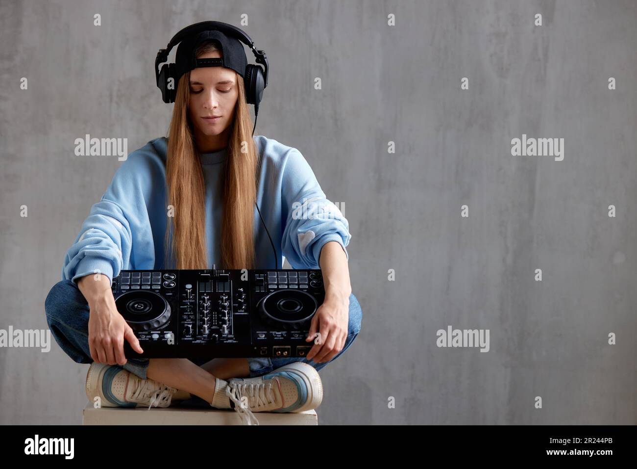 Studio portrait of a young pretty long-haired DJ girl in a blue sweater ...