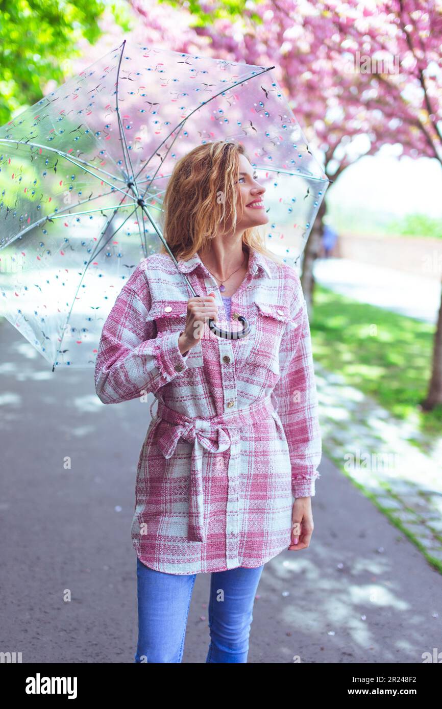 Young 30s Caucasian woman walking in park with transparent umbrella ...