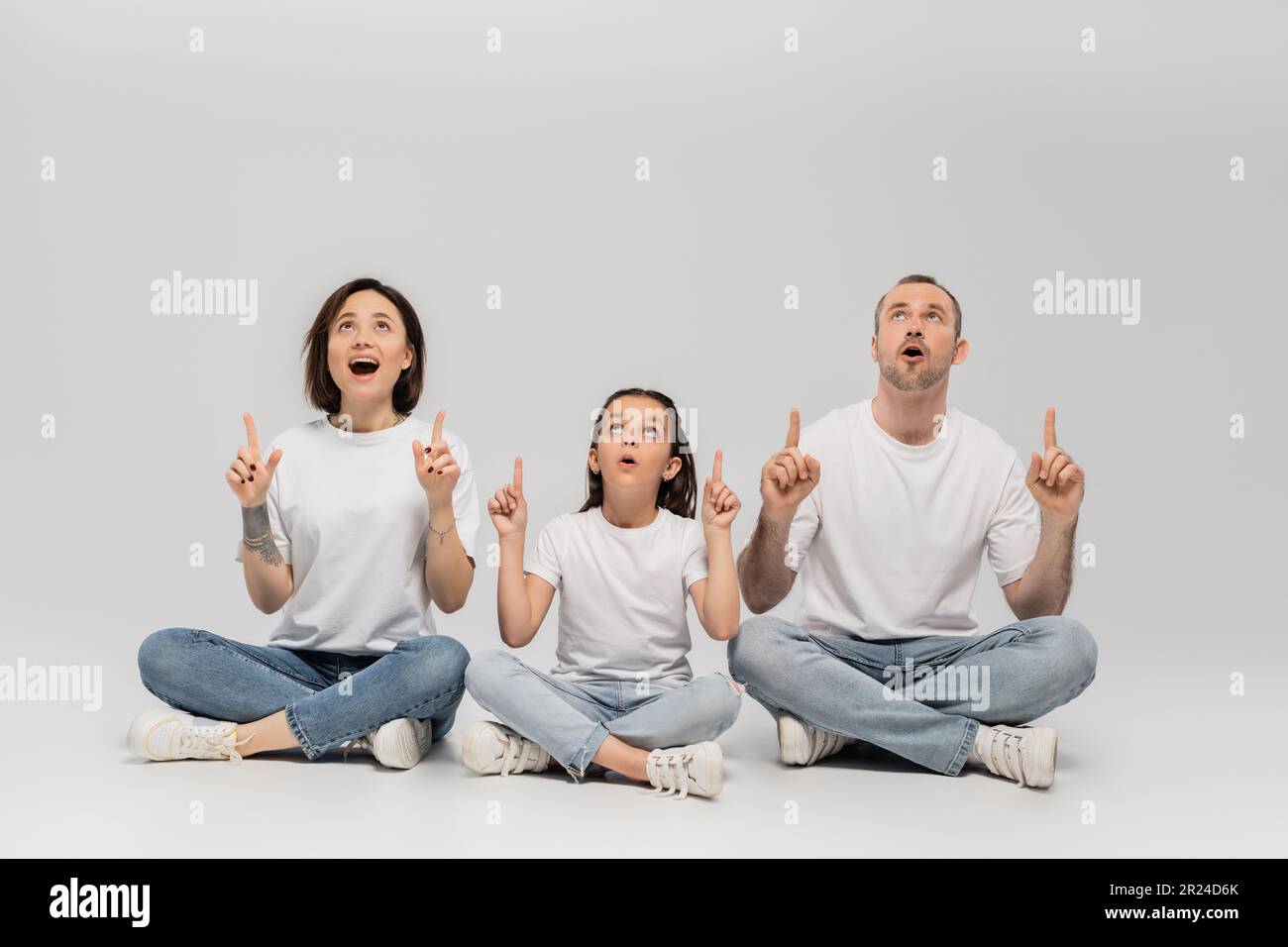 amazed family sitting with crossed legs in white t-shirts and blue ...
