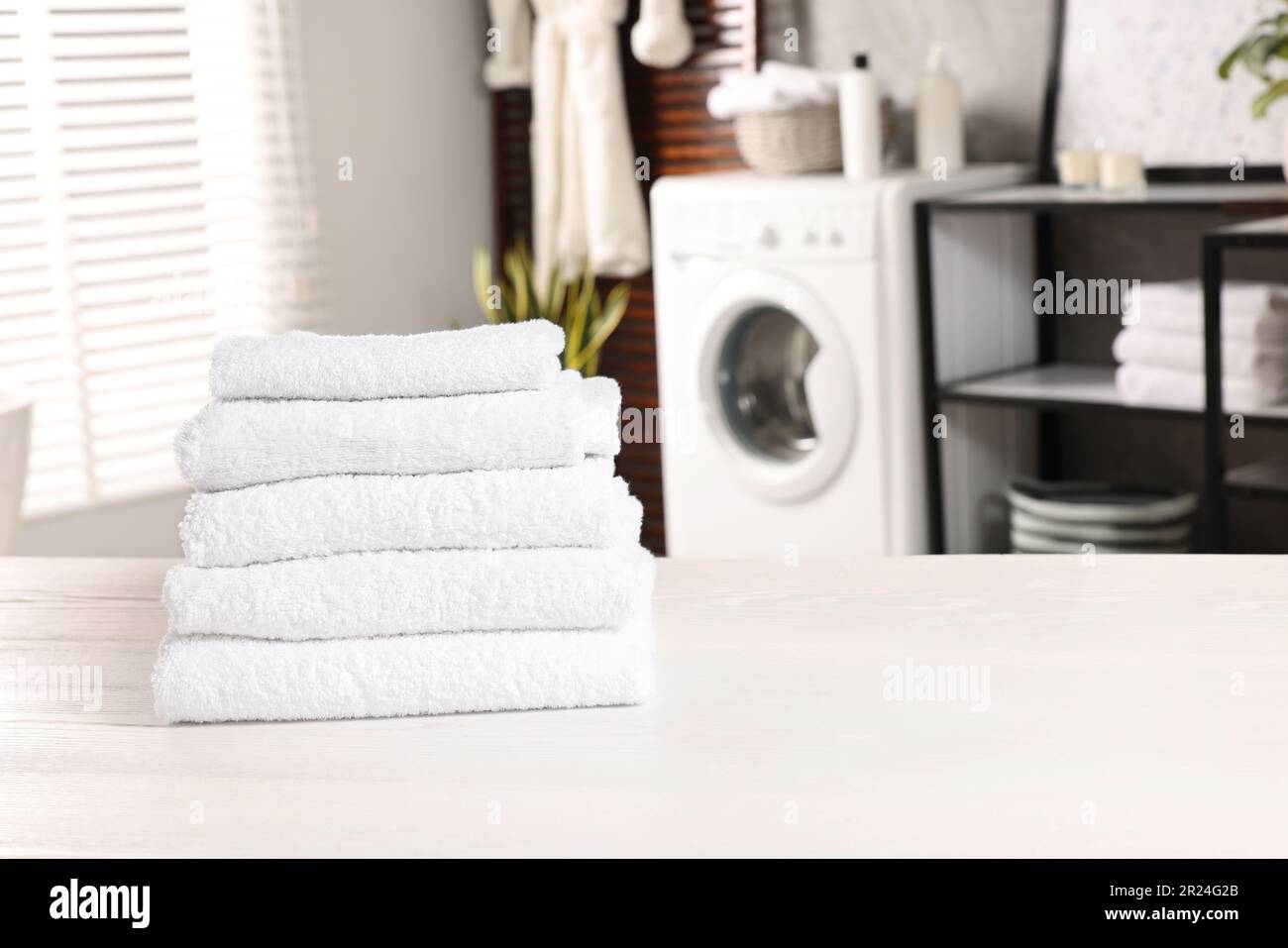 Stack of clean towels on white table in laundry room, space for text ...