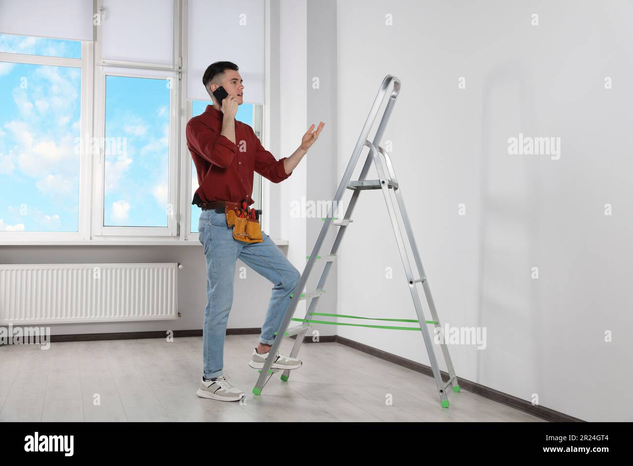 Handyman talking on phone while climbing up stepladder in room Stock ...