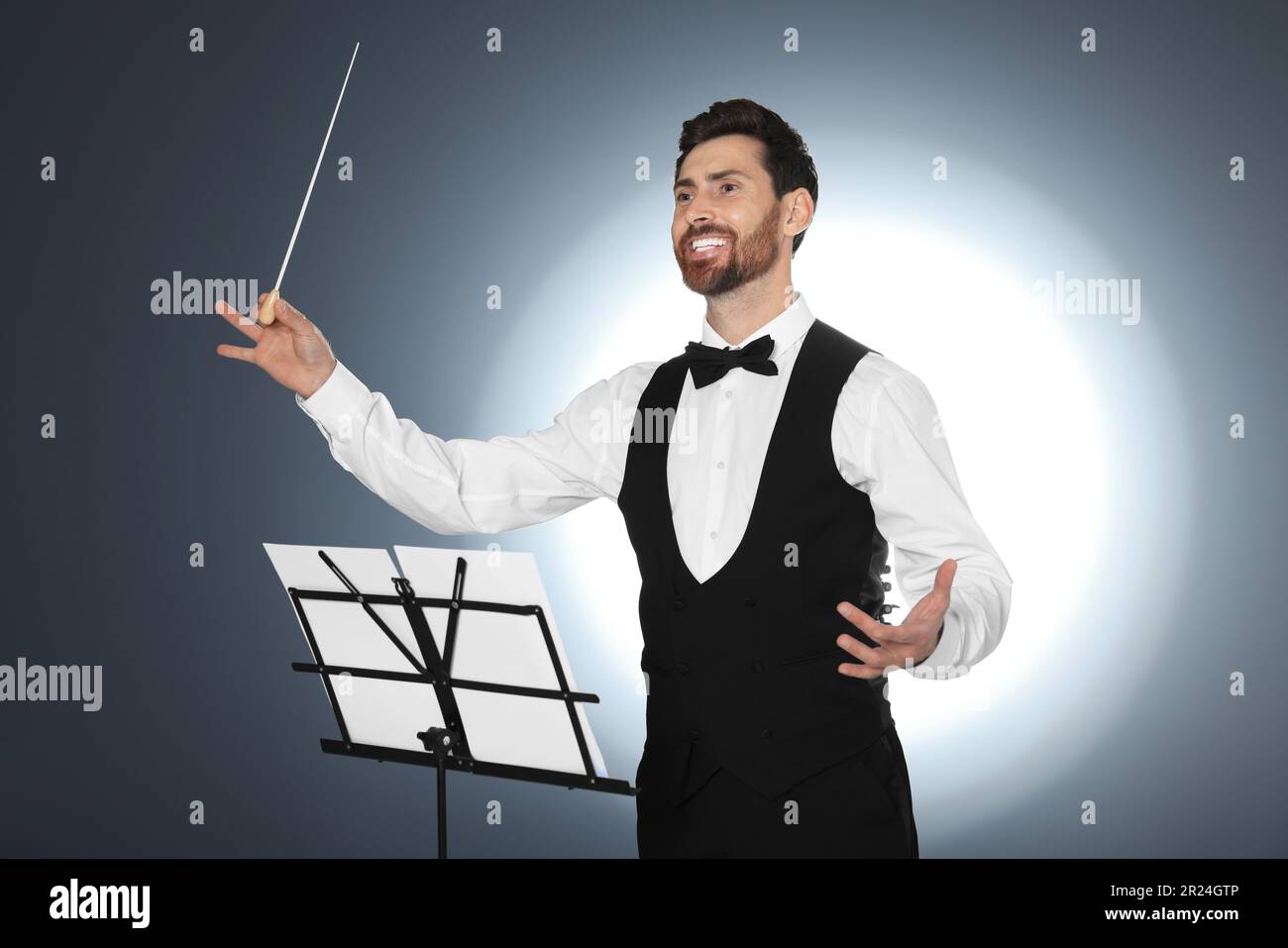 Happy professional conductor with baton and note stand on grey ...