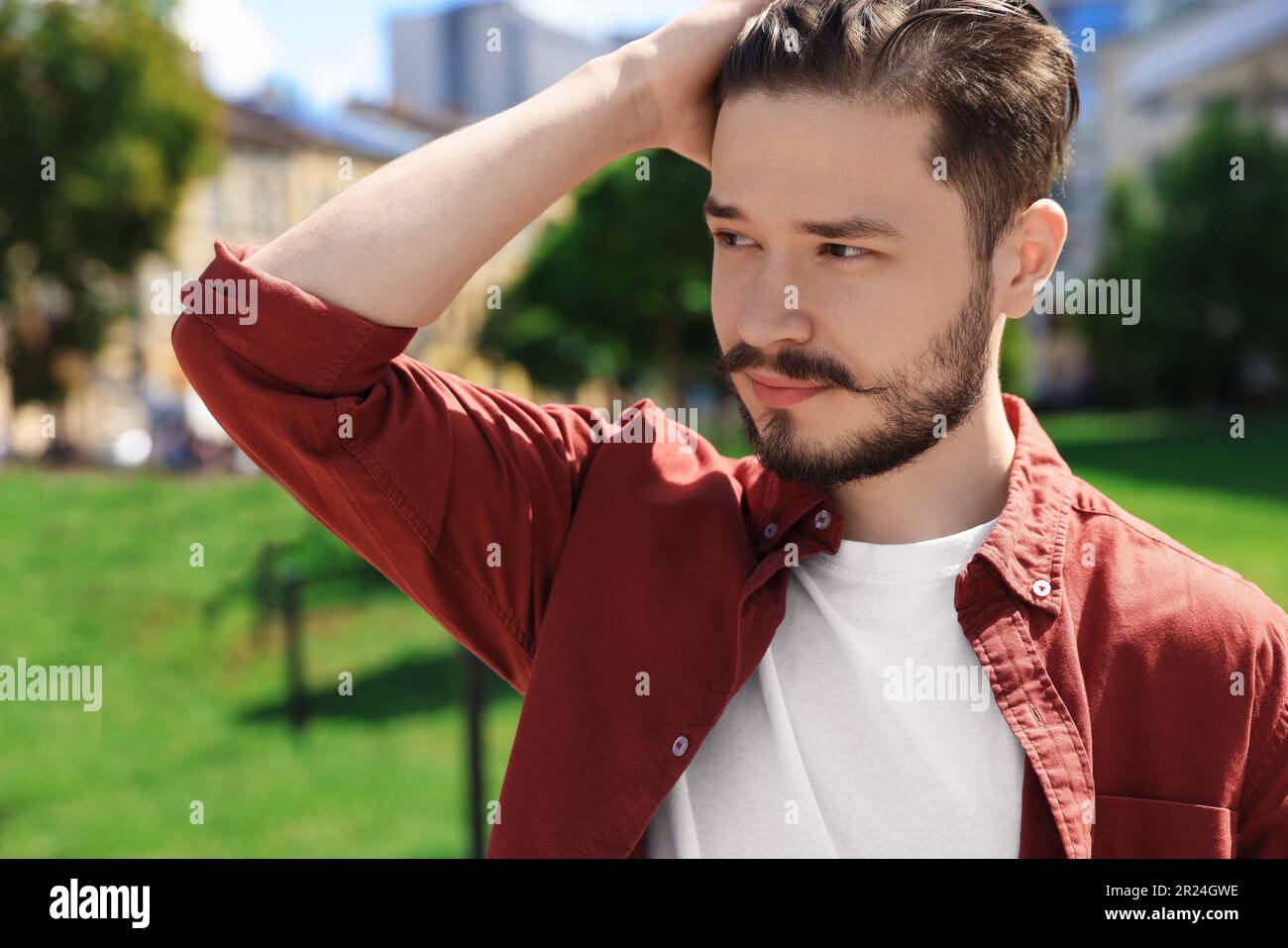 Smiling man touching his head in park Stock Photo - Alamy