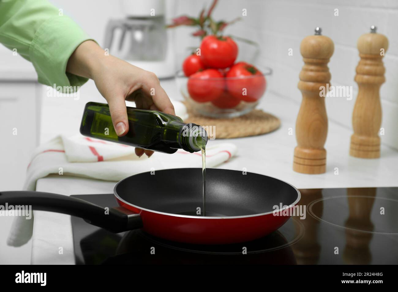 Woman pouring cooking oil from bottle into frying pan in kitchen ...