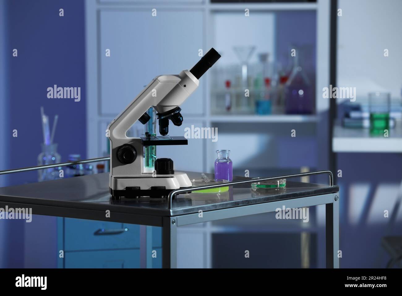 Modern microscope and glassware with colorful liquids on metal table in ...