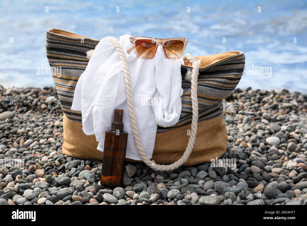 Beautiful bag with sunglasses, sunscreen and white shirt near sea on ...
