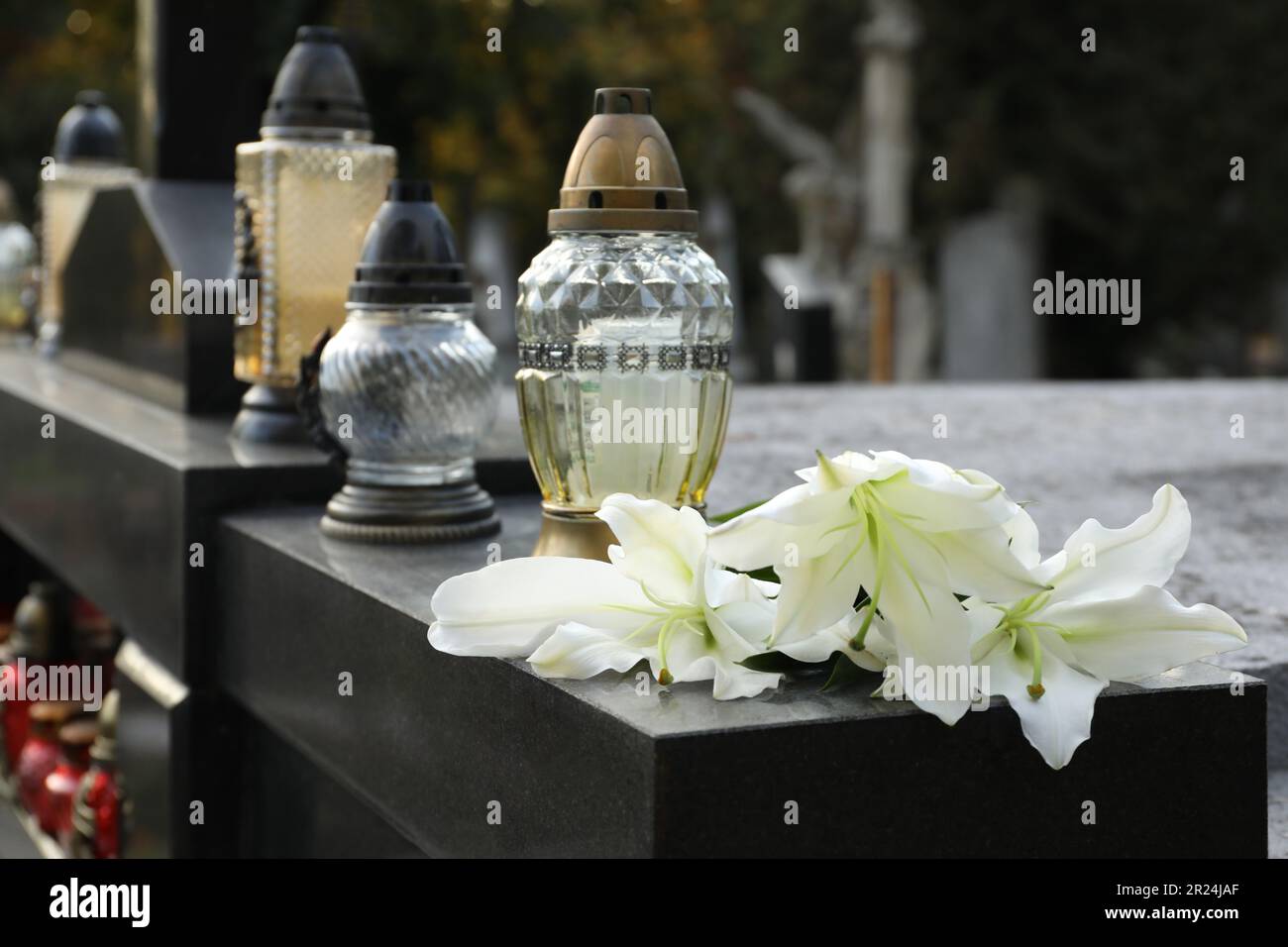 White lilies and grave light on granite tombstone outdoors, space for text. Funeral ceremony ...