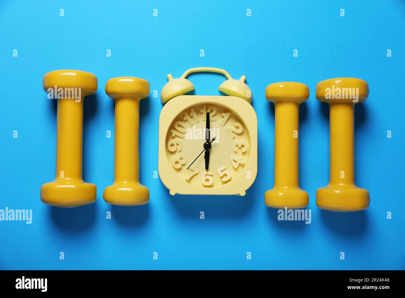Yellow alarm clock and dumbbells on light blue background, flat lay ...