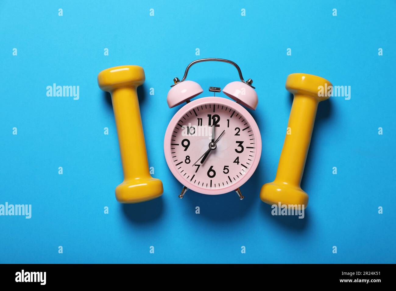 Yellow dumbbells and alarm clock on light blue background, flat lay ...
