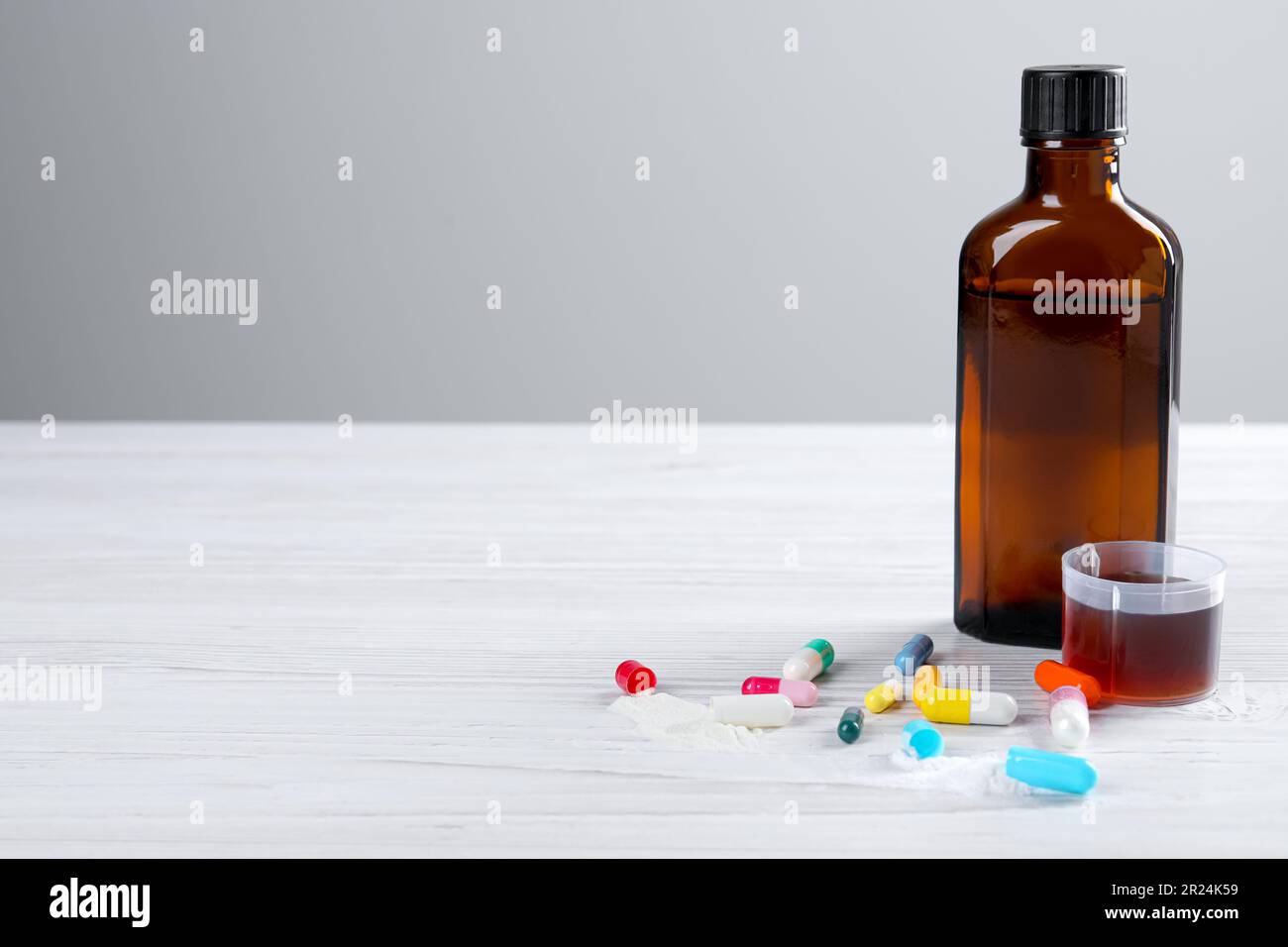 Pills, bottle with measuring cup of syrup on wooden table against white ...