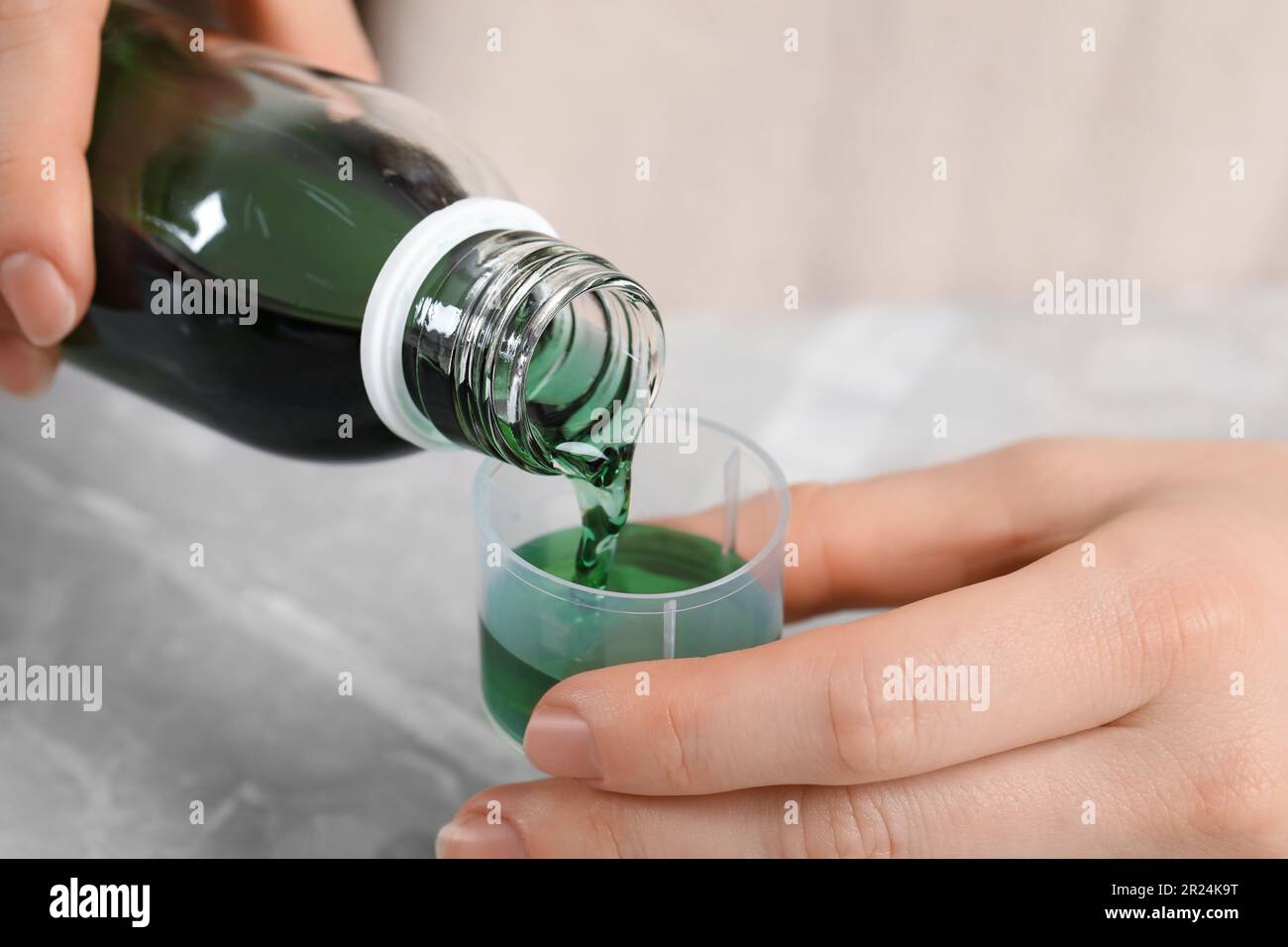 Woman pouring syrup from bottle into measuring cup at grey marble table ...